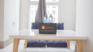 Uma mesa branca com base de madeira, almofada azul e uma bolsa 'Travelio' com duas garrafas de água.