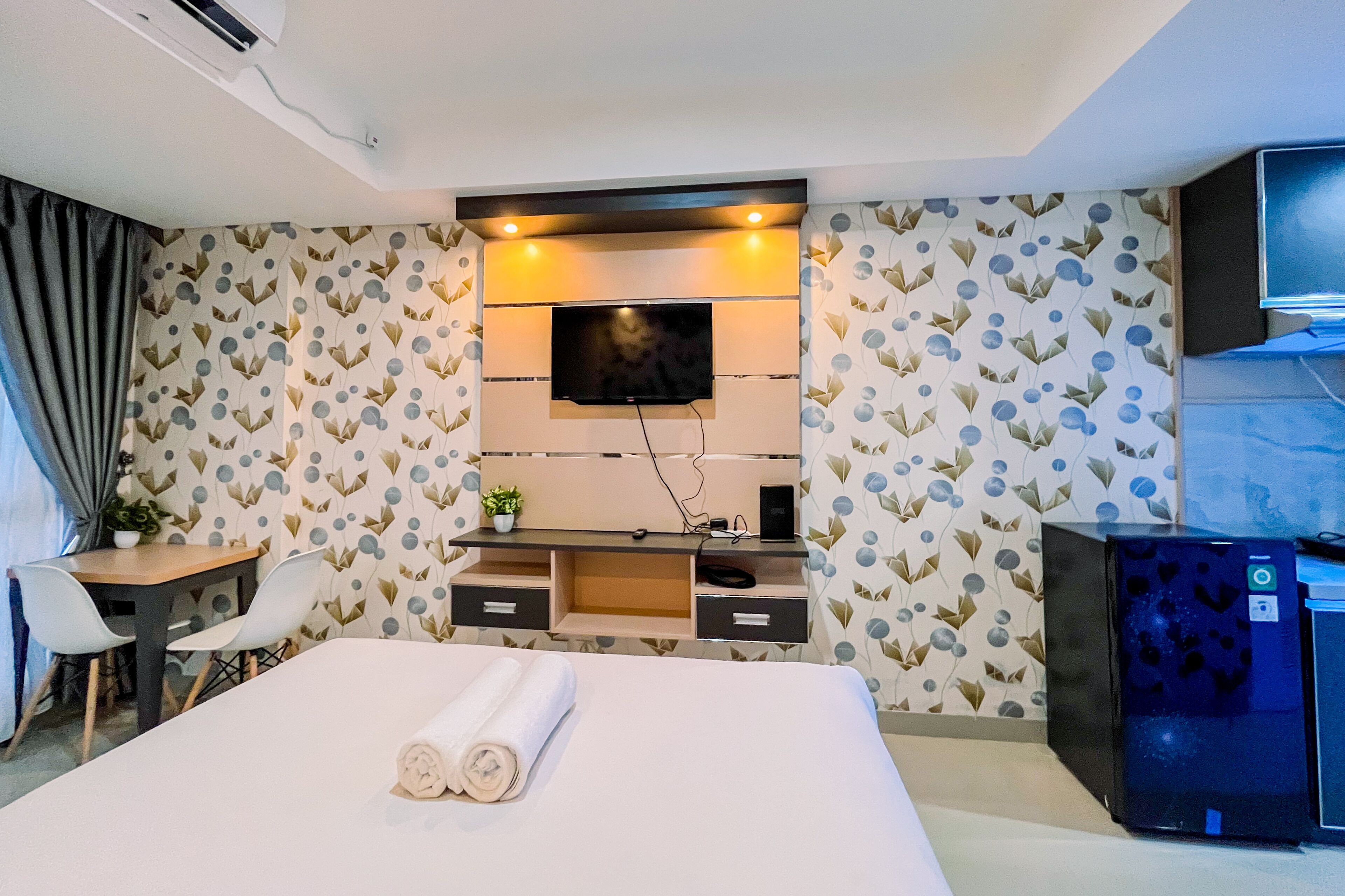 Quarto de hotel com cama, escrivaninha, cadeiras, televisão e minibar.