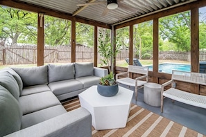 Uma área de estar externa coberta com um sofá modular, uma mesa de centro redonda e uma piscina ao fundo.