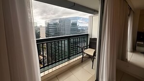 Uma varanda com grade de vidro, uma cadeira e vista para um horizonte urbano com edifícios modernos.