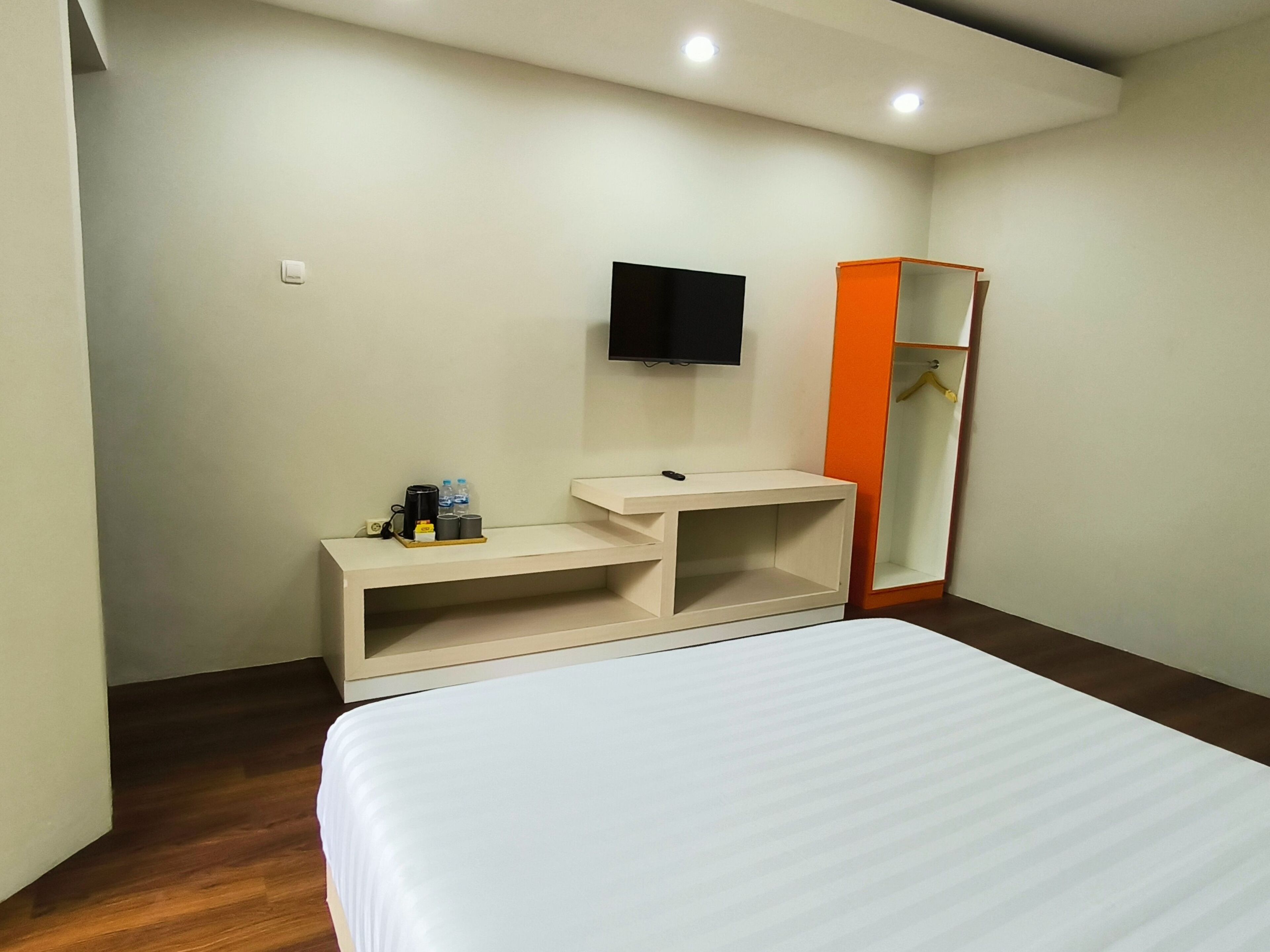 Quarto de hotel com cama, televisão na parede, secretária pequena com cadeira e guarda-roupa.
