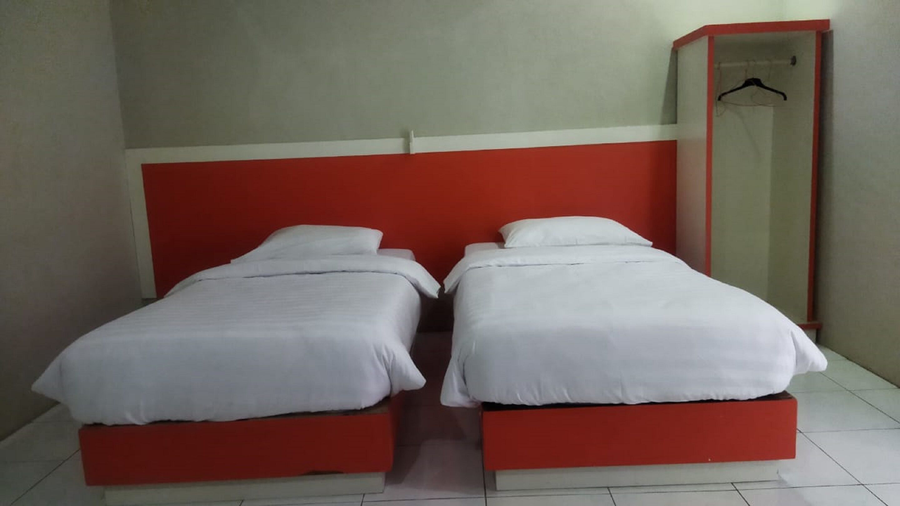 Quarto com duas camas de solteiro, cada uma com roupa de cama branca e cabeceiras vermelhas.