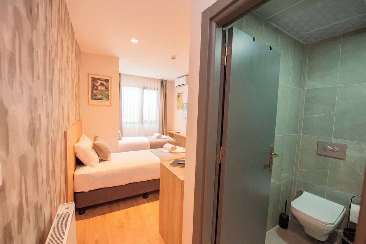 Quarto de hotel com cama, mesa de cabeceira e banheiro com vaso sanitário e chuveiro.