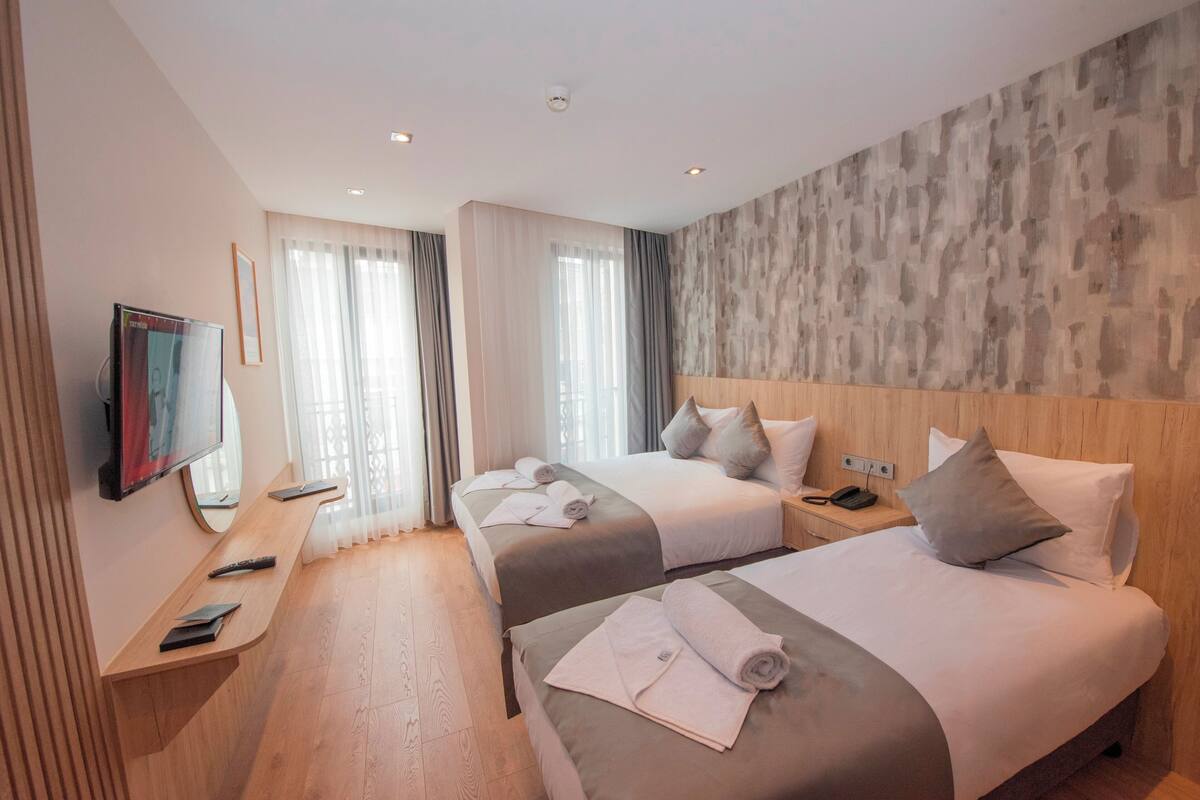 Quarto de hotel com duas camas, televisão, escrivaninha e design moderno na parede.