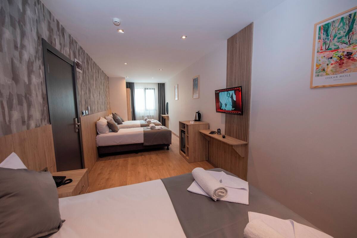 Quarto de hotel com cama, escrivaninha, televisão e banheiro.