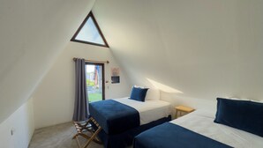 Um quarto pequeno e triangular com duas camas, uma cadeira de madeira e uma janela.