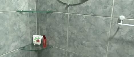 Uma casa de banho com lavatório, espelho e prateleira de vidro com artigos de higiene pessoal.