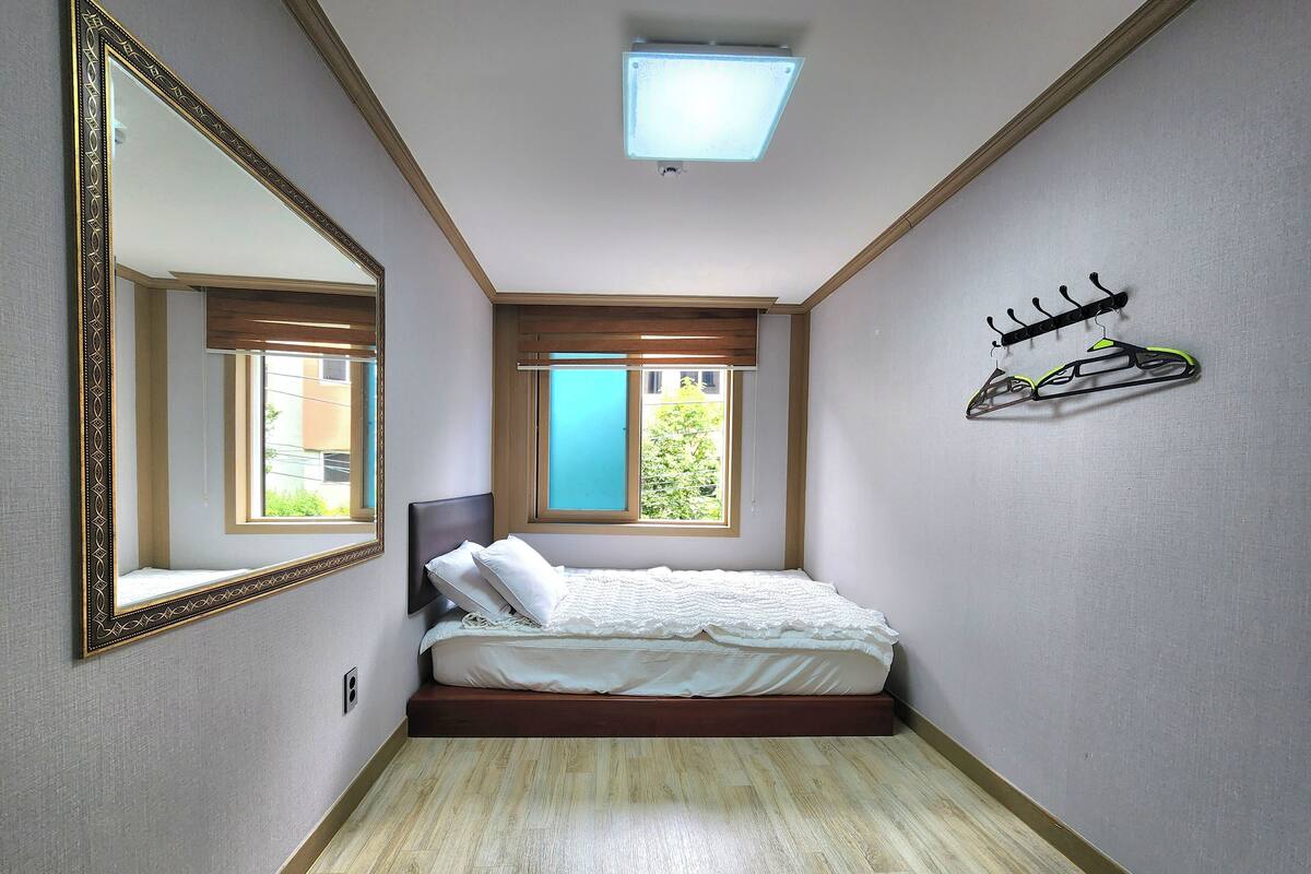 Quarto com cama, espelho grande, janela e luminária no teto.