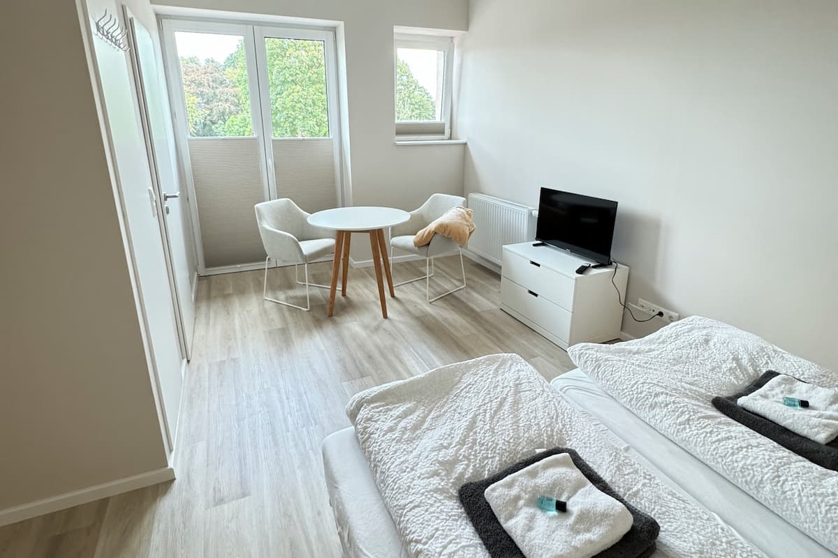 Quarto moderno e bem iluminado, com uma cama, escrivaninha e televisão.