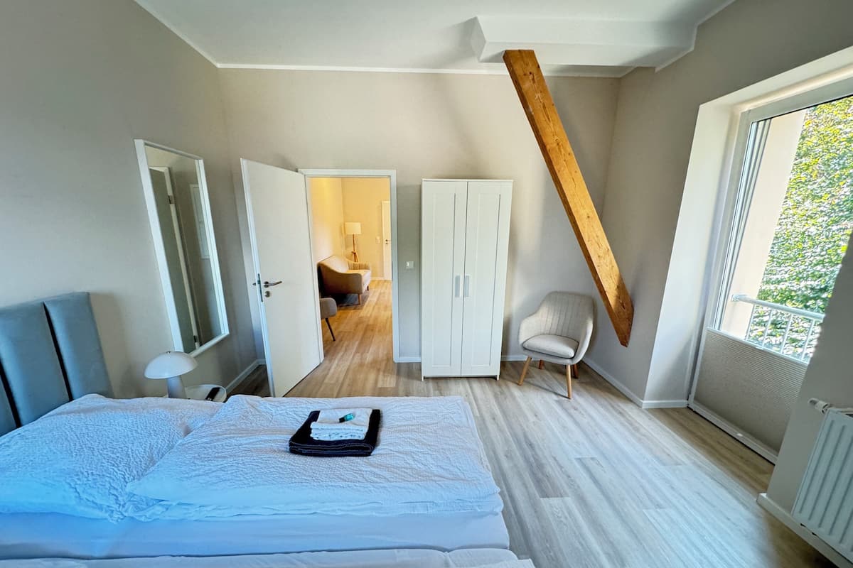 Quarto com cama grande, guarda-roupa, cadeira e vista para uma varanda.