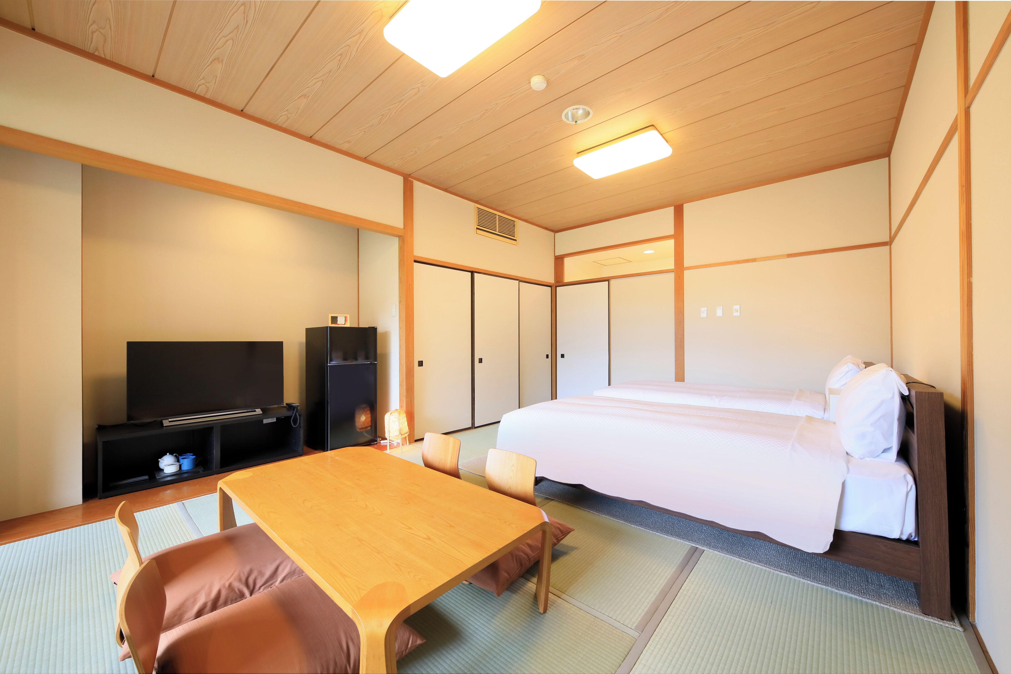 Quarto de hotel com cama, televisão, mesa de madeira e área de estar.