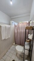 Um banheiro pequeno com vaso sanitário, cortina de chuveiro e prateleira com toalhas e produtos de higiene pessoal.