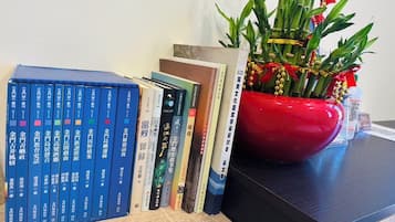 Uma estante com livros e um vaso vermelho com plantas verdes.