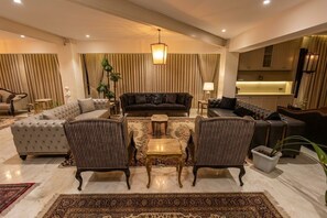 Uma sala de estar ampla, com sofá, poltronas, mesa de centro e um lustre.