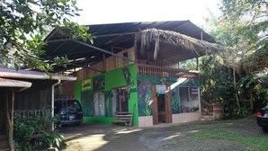 Um edifício com fachada verde e telhado de colmo. Há uma área de recepção com um aviso, e um banco do lado de fora.