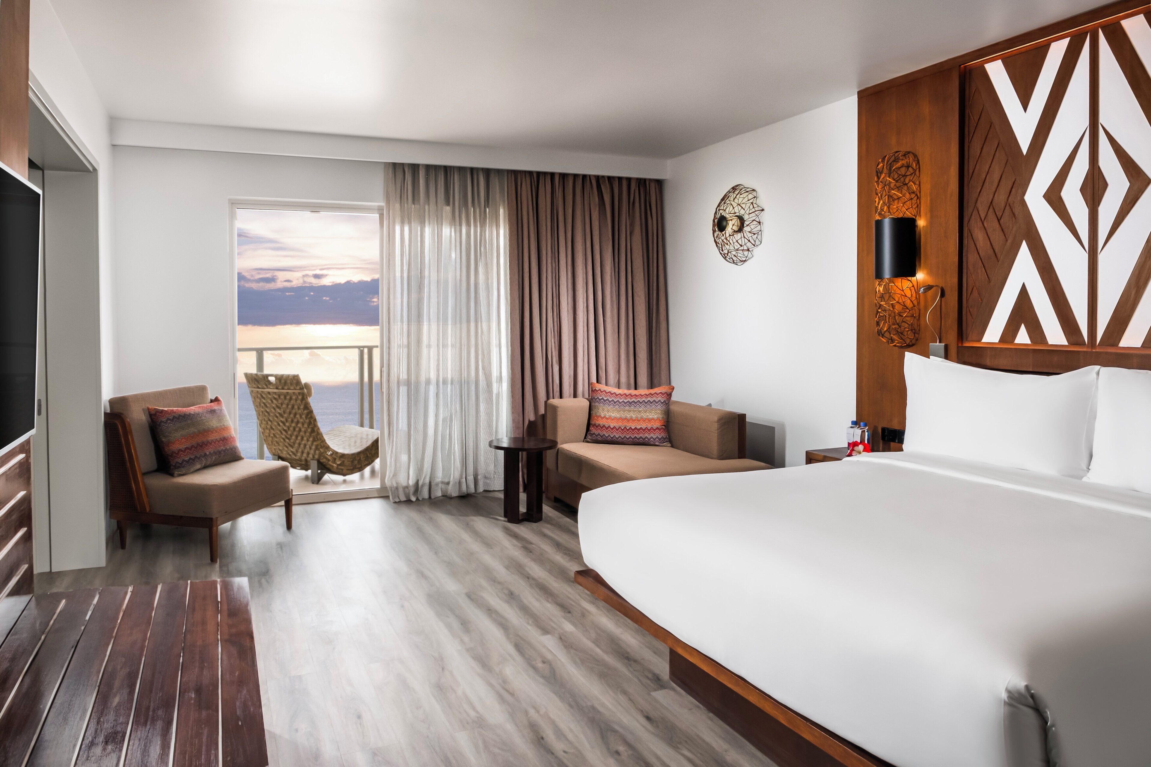 Quarto de hotel com uma cama grande, um sofá, uma cadeira, uma mesa pequena e vista para o mar pela janela.