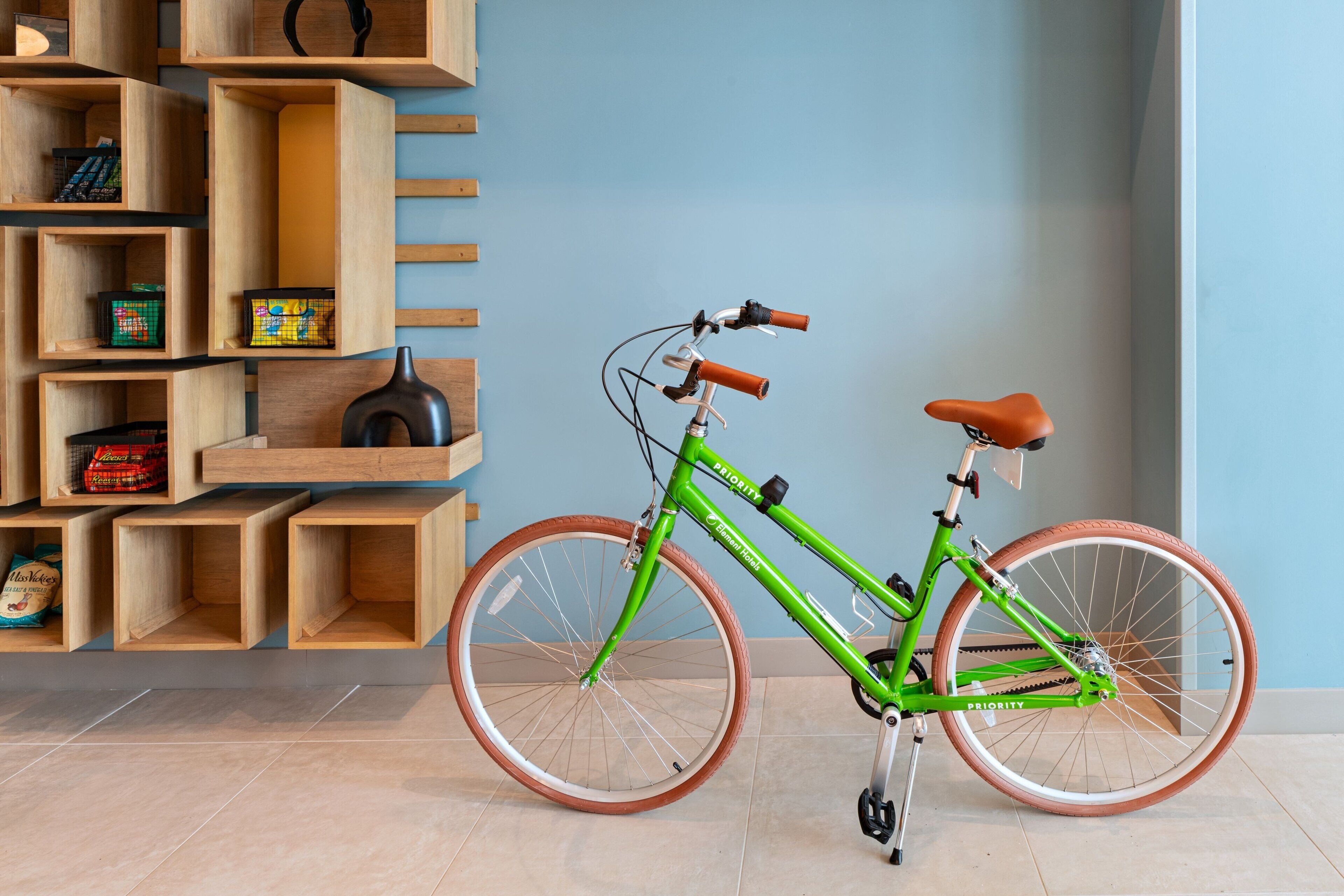 Uma bicicleta verde com detalhes em castanho, prateleiras de madeira com vários objetos e uma parede azul.