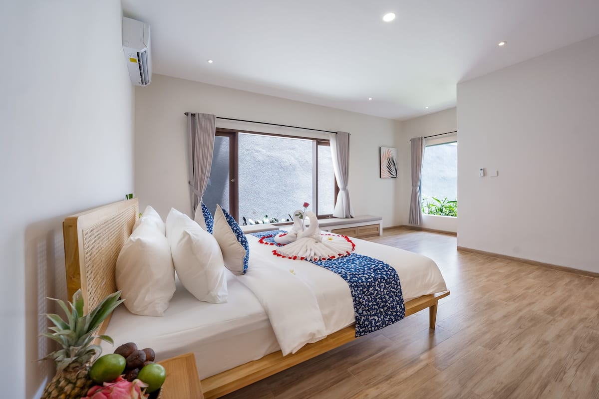 Um quarto espaçoso com uma cama grande, cabeceira de madeira e vista para o exterior através de janelas amplas.