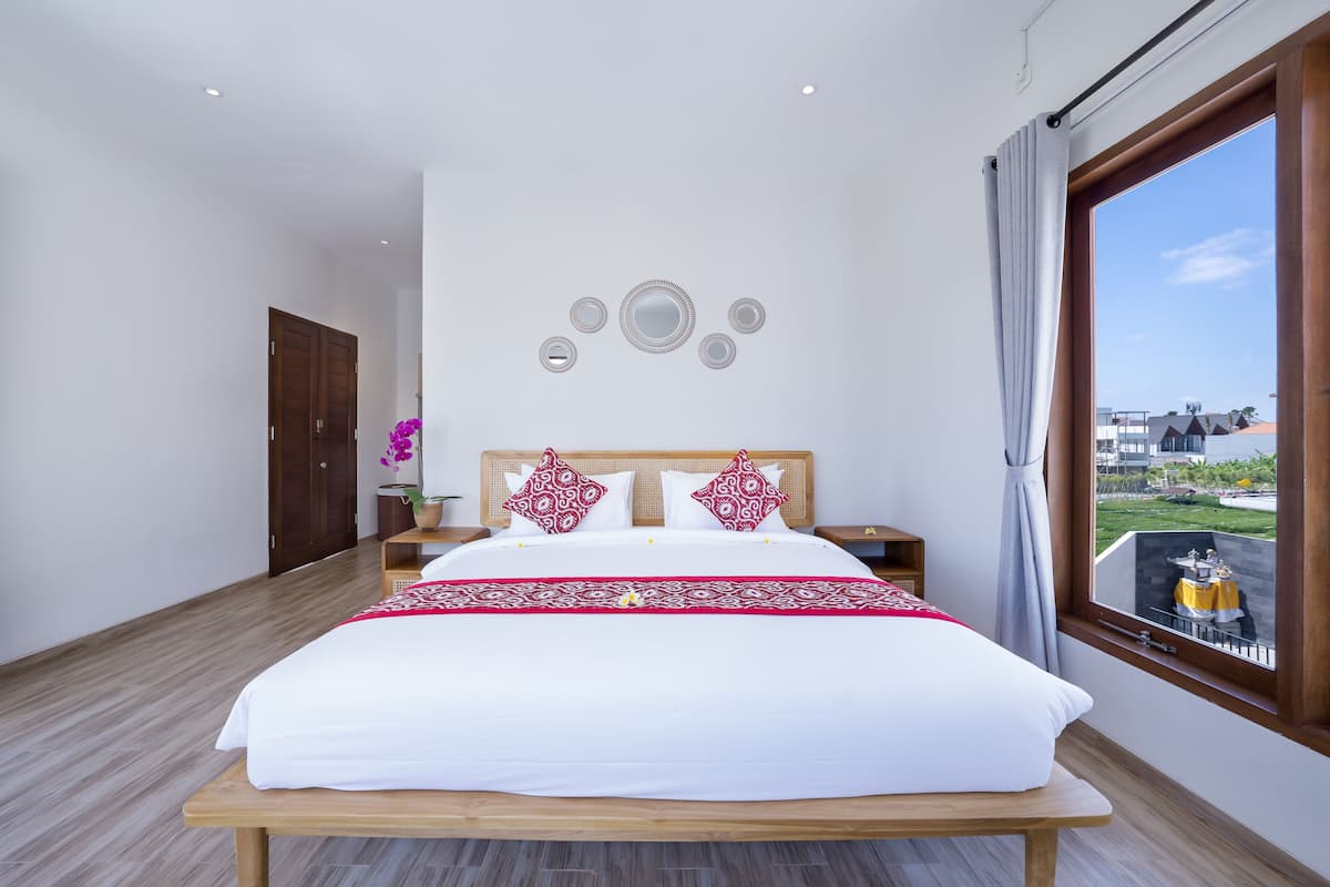Quarto de hotel moderno com uma cama grande, cabeceira de madeira e vista para a cidade através de uma janela ampla.