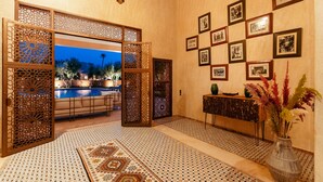 Um saguão com vista para a piscina, painéis decorativos, um tapete estampado e quadros nas paredes.