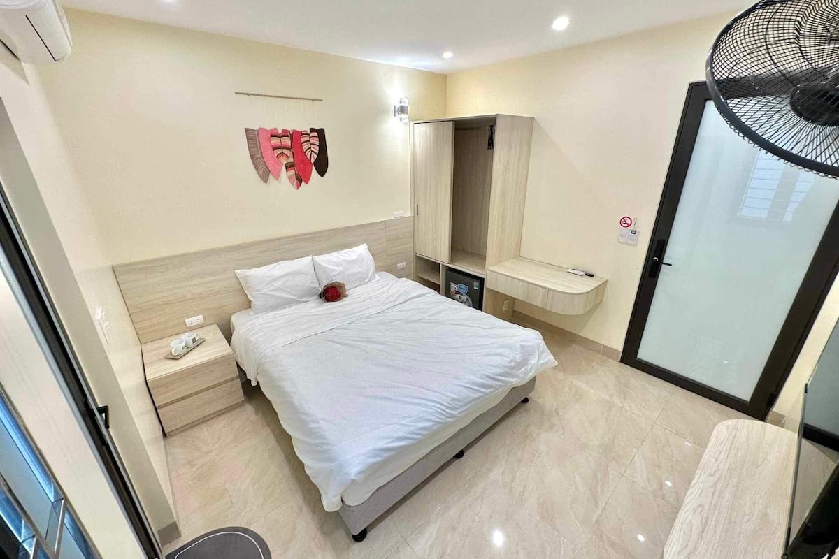 Quarto de hotel moderno com cama, mesa de cabeceira e pequena escrivaninha com cadeira.