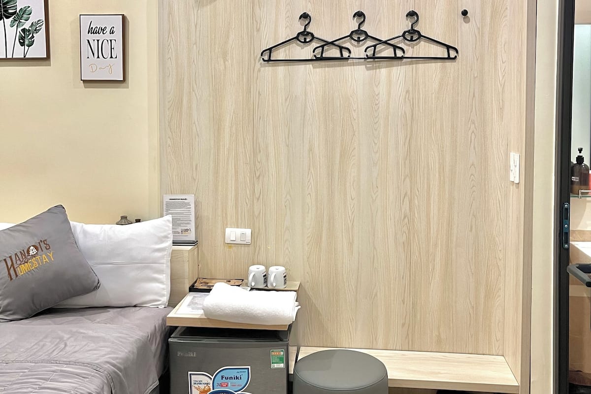 Quarto moderno com cama, uma mesinha com chaleira, um banco e um cabideiro fixado na parede.