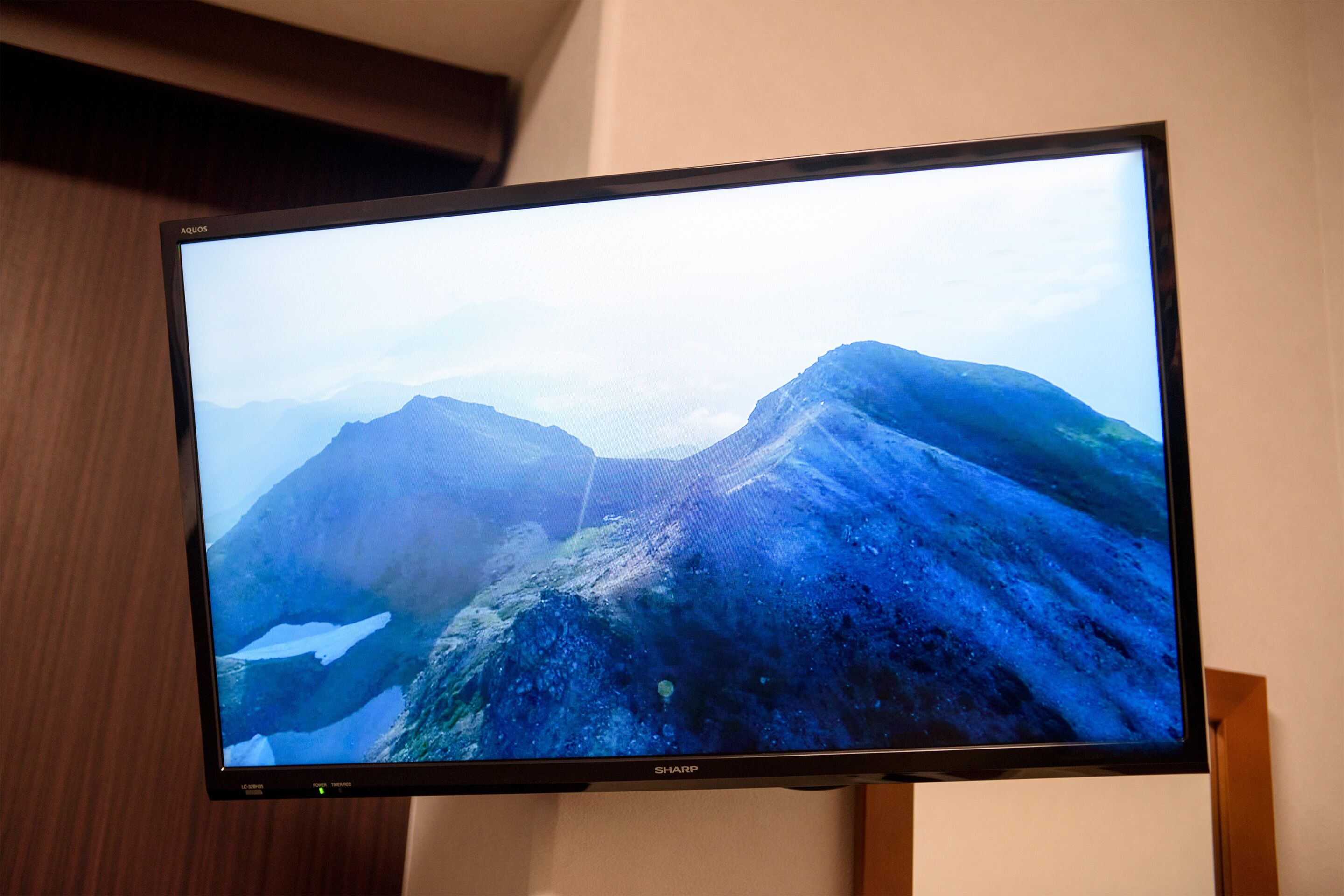 Televisão de tela plana presa em um suporte de madeira exibindo uma paisagem montanhosa.