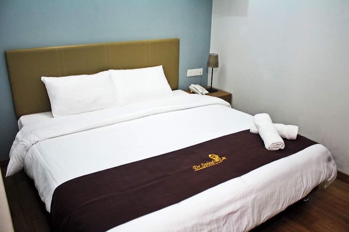 Cama bem arrumada com lençóis brancos e detalhes em castanho, telefone ao lado da cama e luminária fixada na parede.