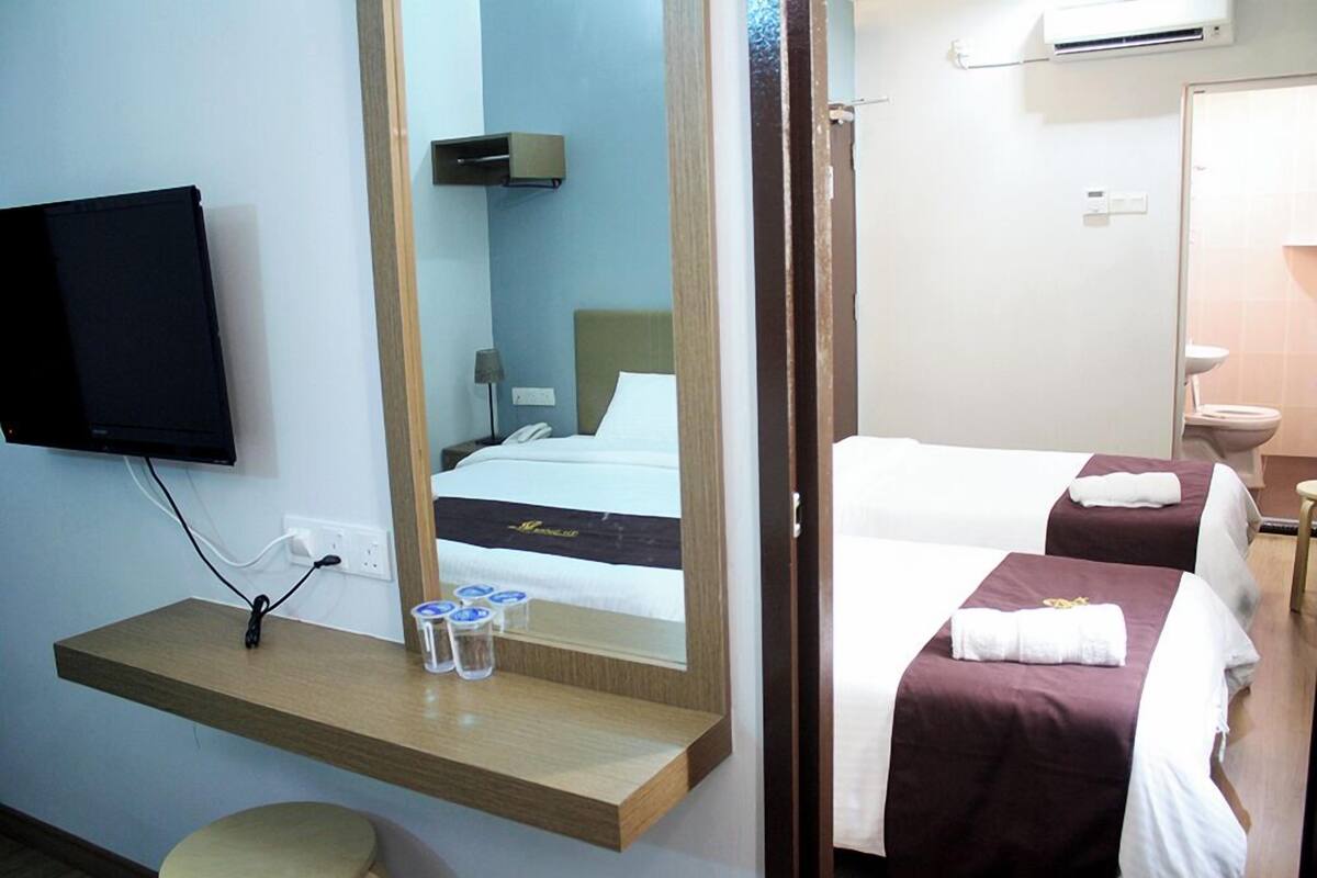 Quarto de hotel com cama, televisão na parede, mesa de cabeceira com abajur e espelho.