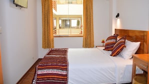 Quarto de hotel com uma cama grande, cabeceira de madeira, mesa de cabeceira e janela com cortinas.