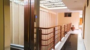 Um corredor de hotel moderno com piso preto brilhante, um elevador de metal e teto estampado.