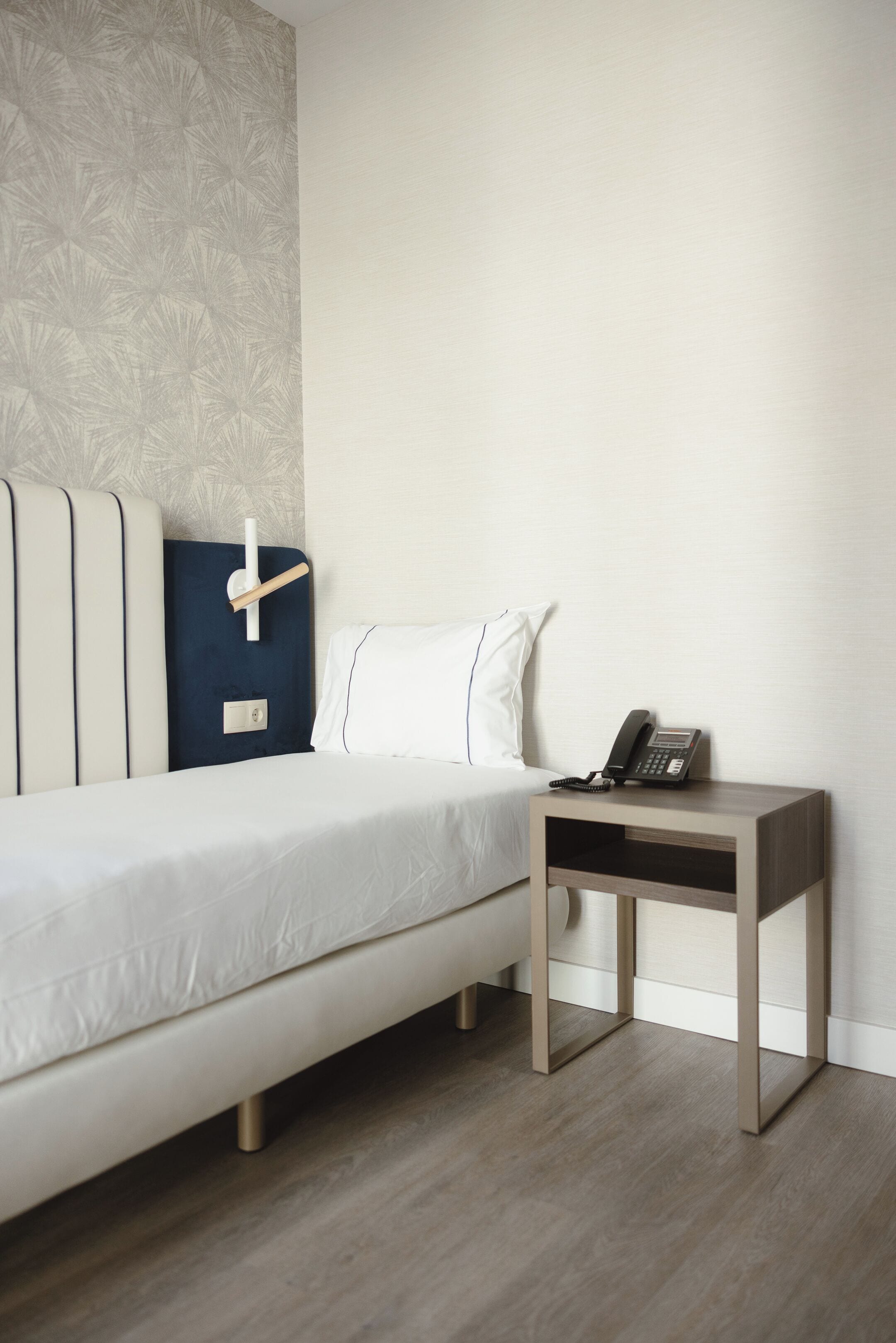 Quarto de hotel moderno com uma cama, mesa de cabeceira com telefone e parede com padrão de folha.