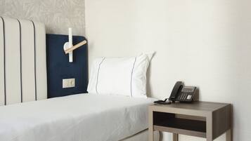 Quarto de hotel moderno com uma cama, mesa de cabeceira com telefone e parede com padrão de folha.