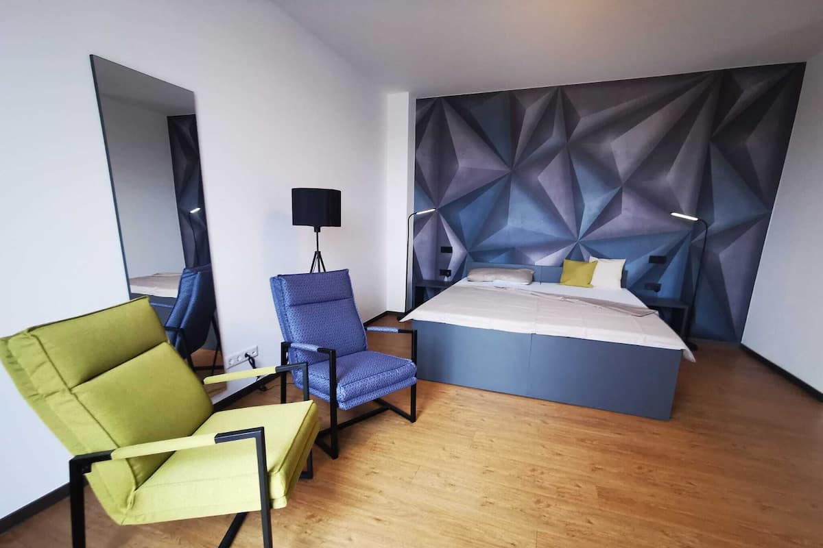 Quarto de hotel moderno com uma cama grande, uma escrivaninha, uma cadeira e um espelho.