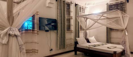 Quarto com cama, cortinas, televisão e ventoinha no teto.
