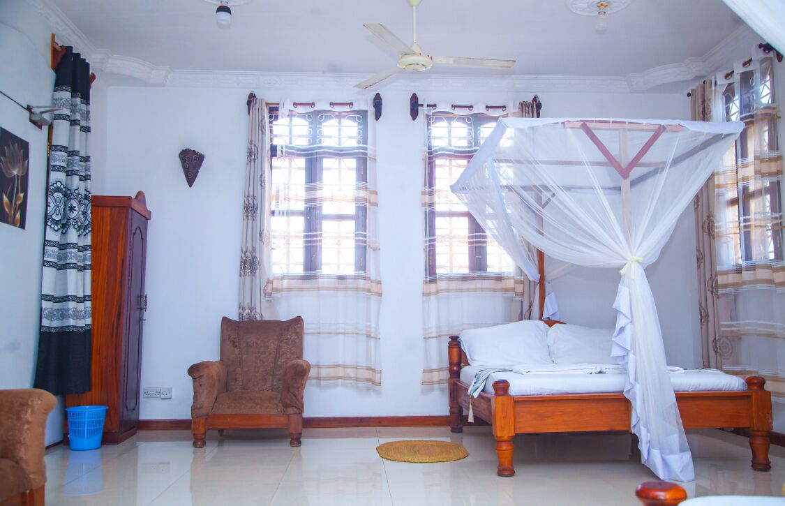 Quarto com cama, cadeira, ventilador de teto e cortinas.