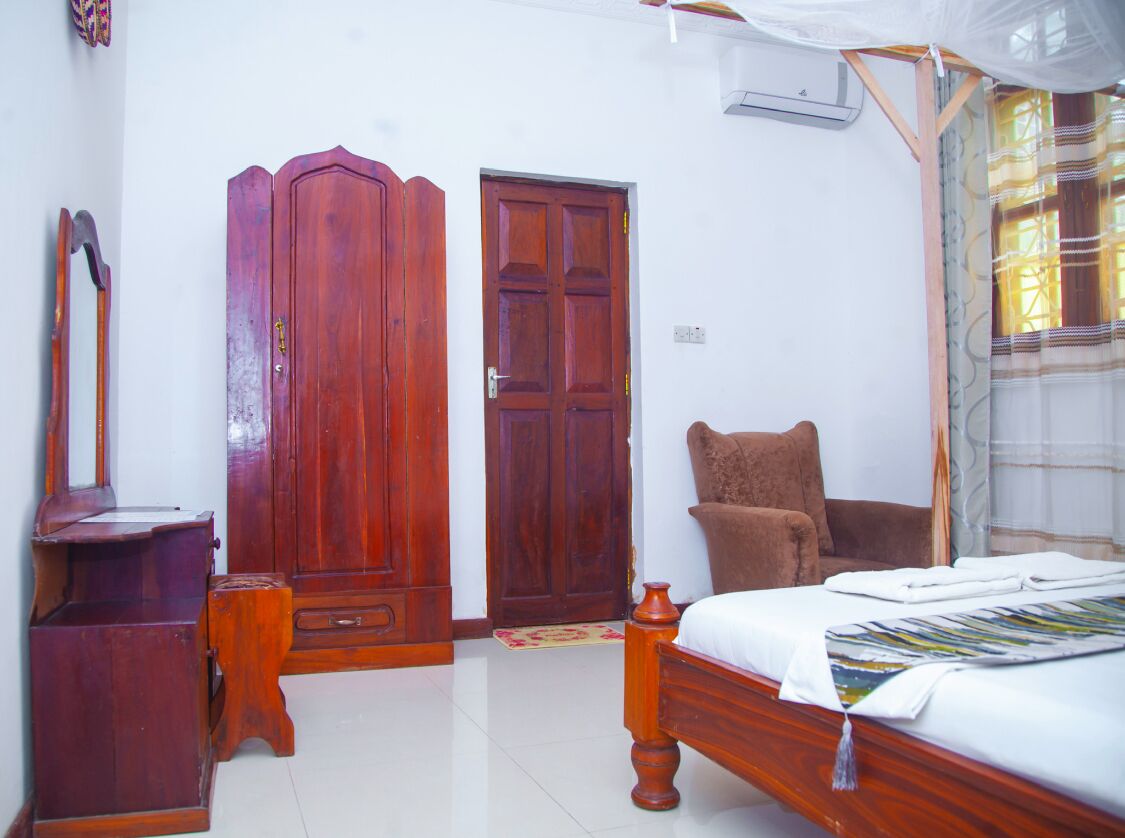 Quarto com cama de madeira, guarda-roupa, espelho e uma cadeira.