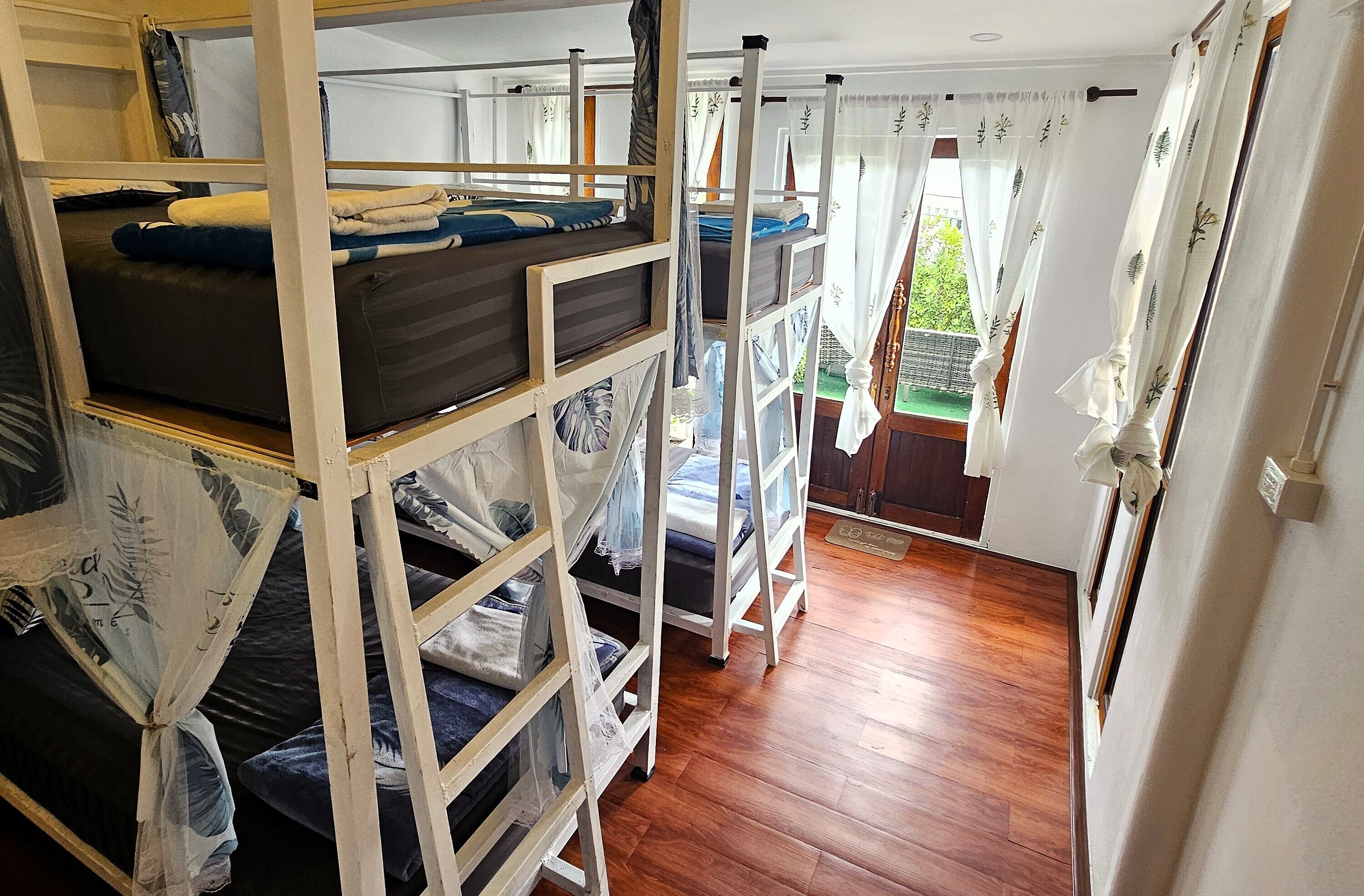 Quarto com beliches, piso de madeira e vista para o verde lá fora.