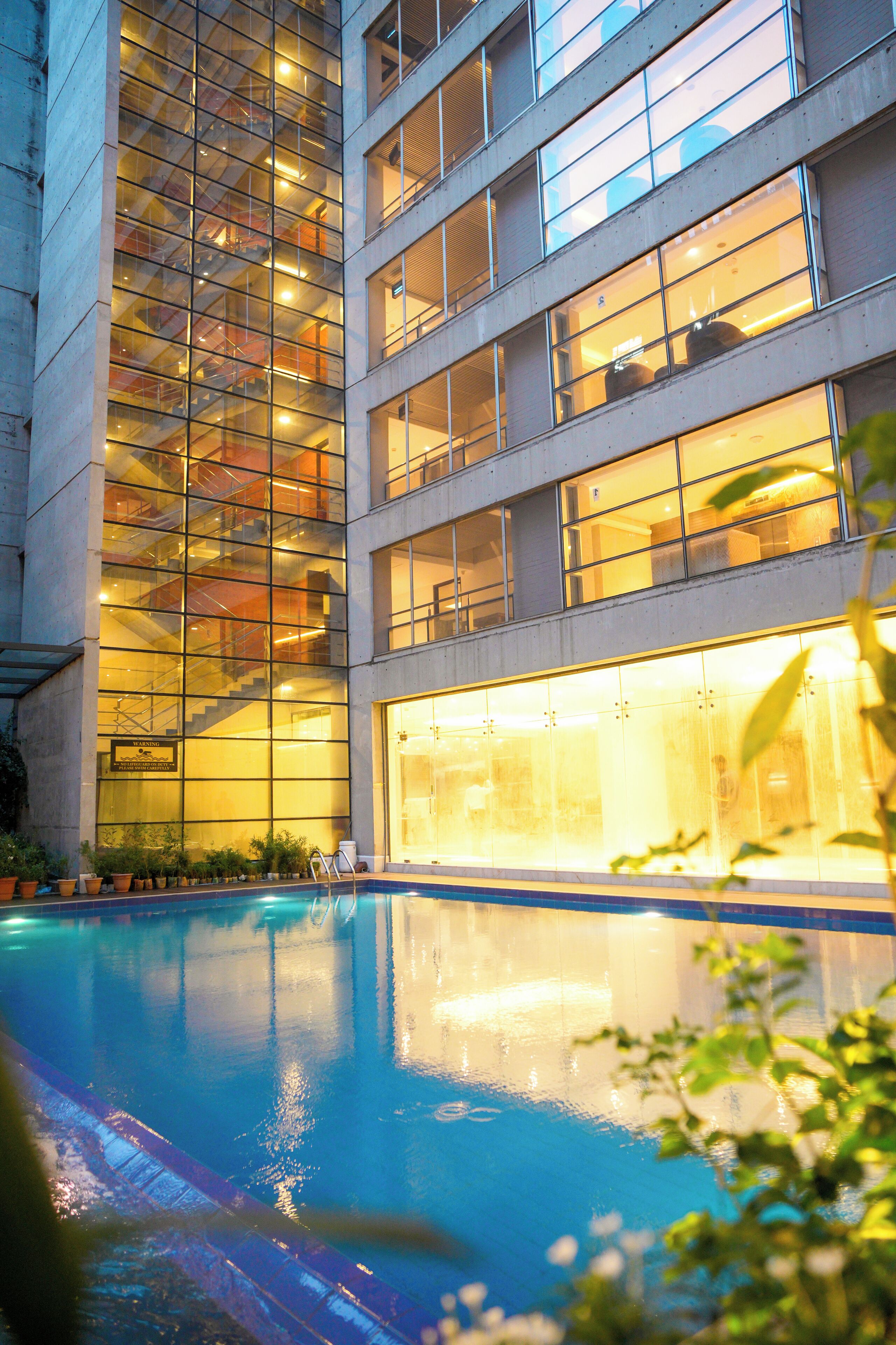 Um edifício moderno com fachada de vidro, piscina e interior bem iluminado.