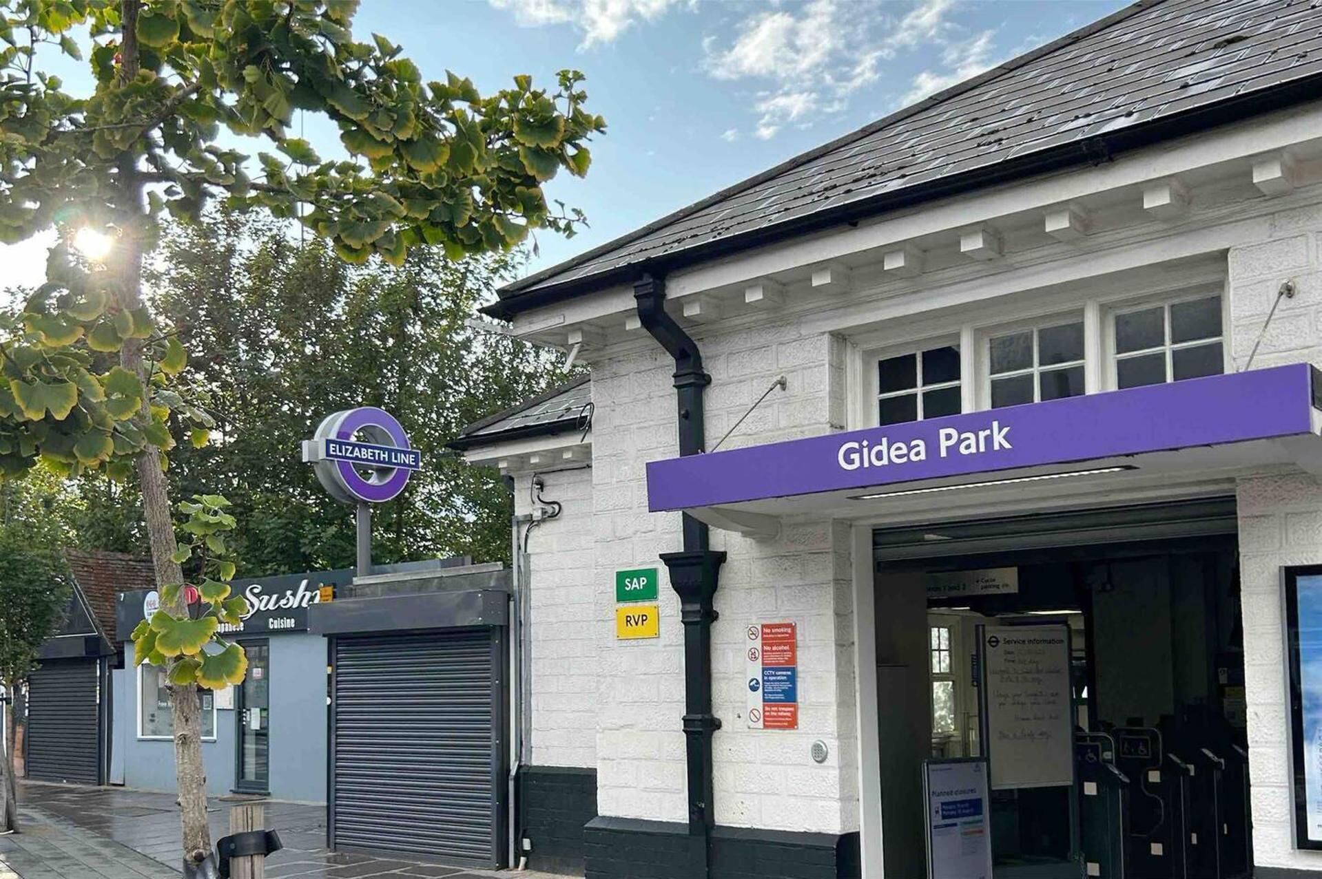 Um edifício com uma placa roxa que diz "Gidea Park" e uma placa para a estação de metro "Elizabeth Line".
