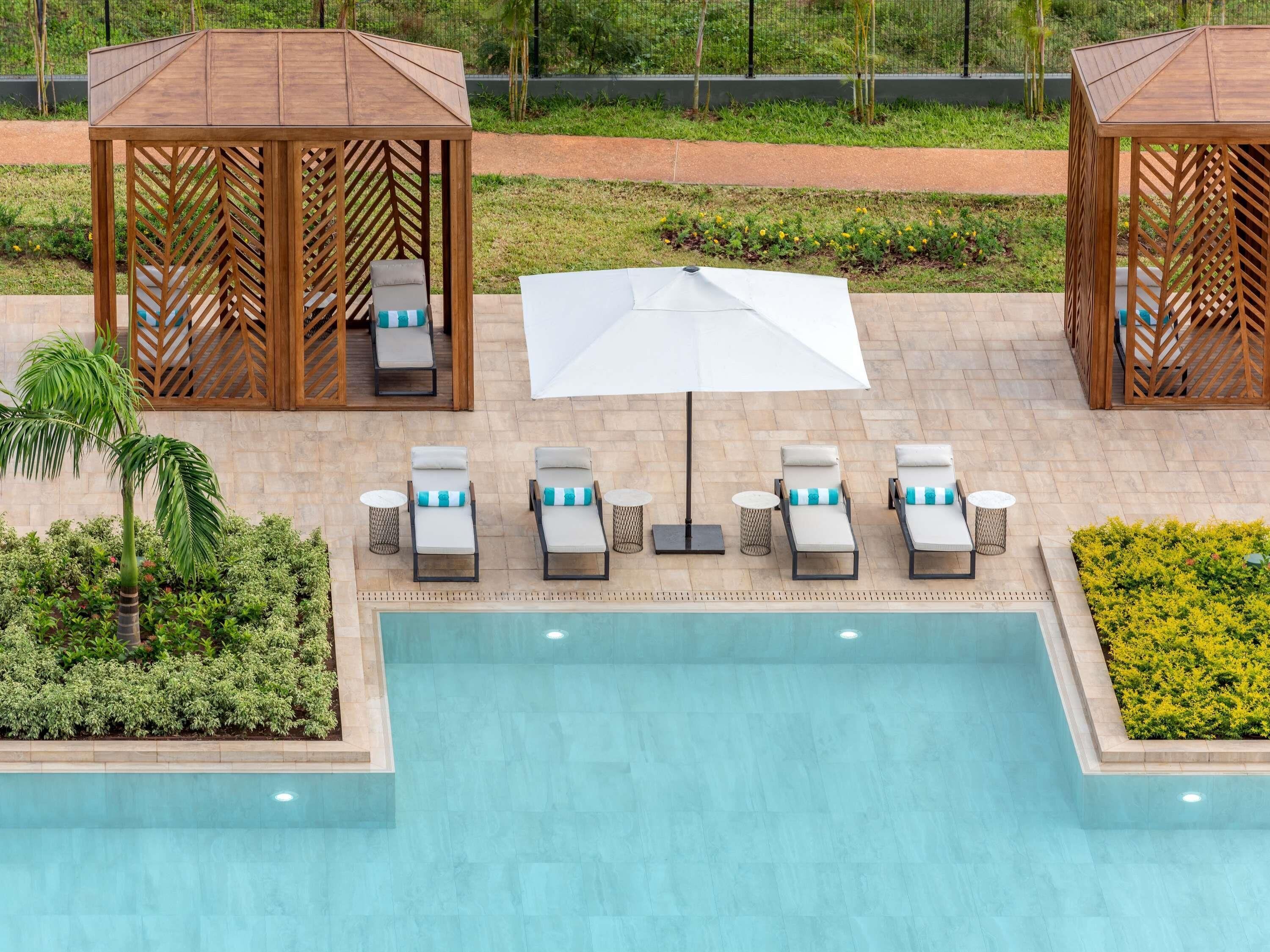 Uma área de piscina no terraço com espreguiçadeiras, guarda-sol e pérgulas de madeira.