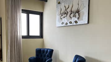 Quarto com duas poltronas azuis, uma janela com cortinas e uma obra de arte pendurada na parede.