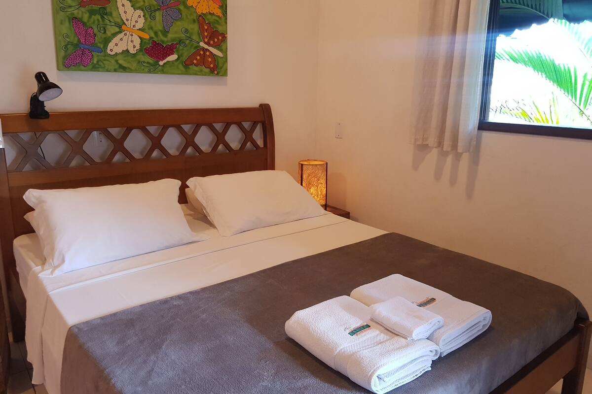 Uma cama bem arrumada com lençóis brancos, cabeceira marrom e um quadro decorativo de borboleta acima.