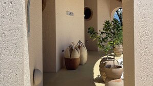 Uma porta em arco que dá para um quarto com uma placa escrita "Tahiti", plantas em vasos e grandes cestos trançados.