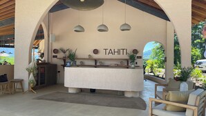 Uma área de recepção com uma placa que diz “TAHITI”, um balcão, luminárias pendentes e vista para o exterior.