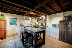 Uma cozinha rústica com uma ilha central, banquetas de madeira e piso de pedra.
