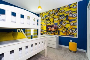Quarto de criança com beliches, parede decorada com o tema Minions e um banquinho pequeno.