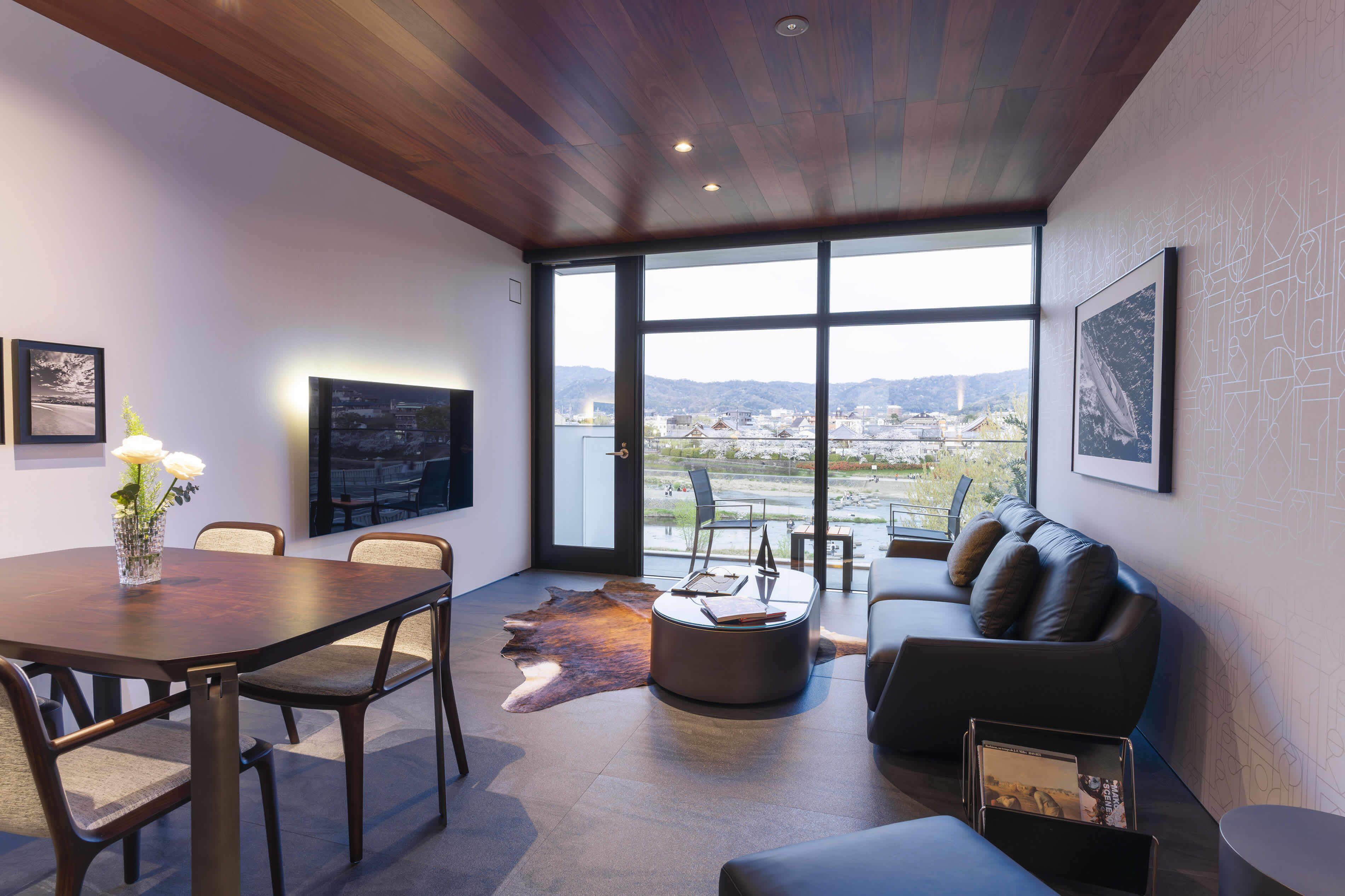 Uma sala de estar moderna com uma janela grande, uma mesa de centro redonda, um sofá e uma mesa de jantar com cadeiras.
