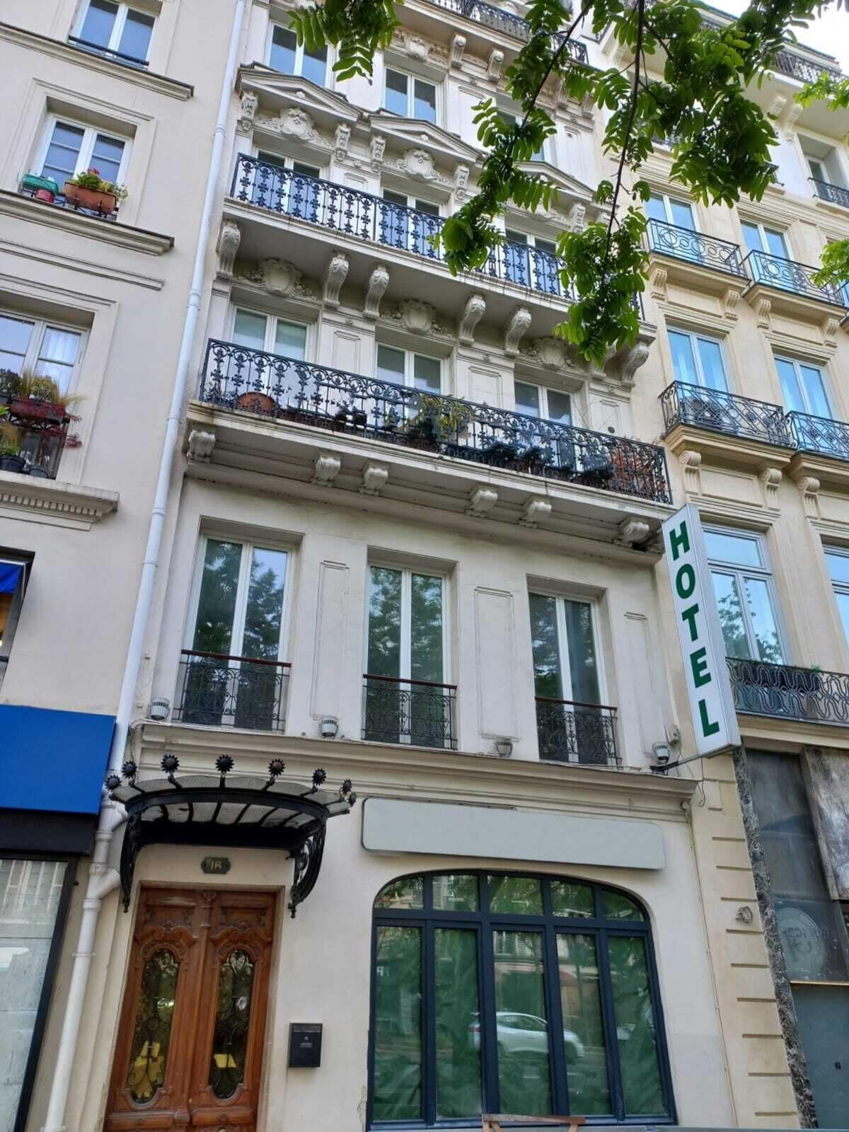 Fachada de hotel com estilo arquitetônico clássico, apresentando várias varandas com grades de ferro forjado, janelas amplas e um letreiro chamativo com a palavra 'HOTEL'.