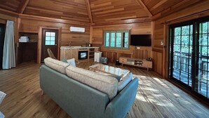 Interior acolhedor de uma cabana de madeira, com sofá, mesa de centro, televisão e cozinha.